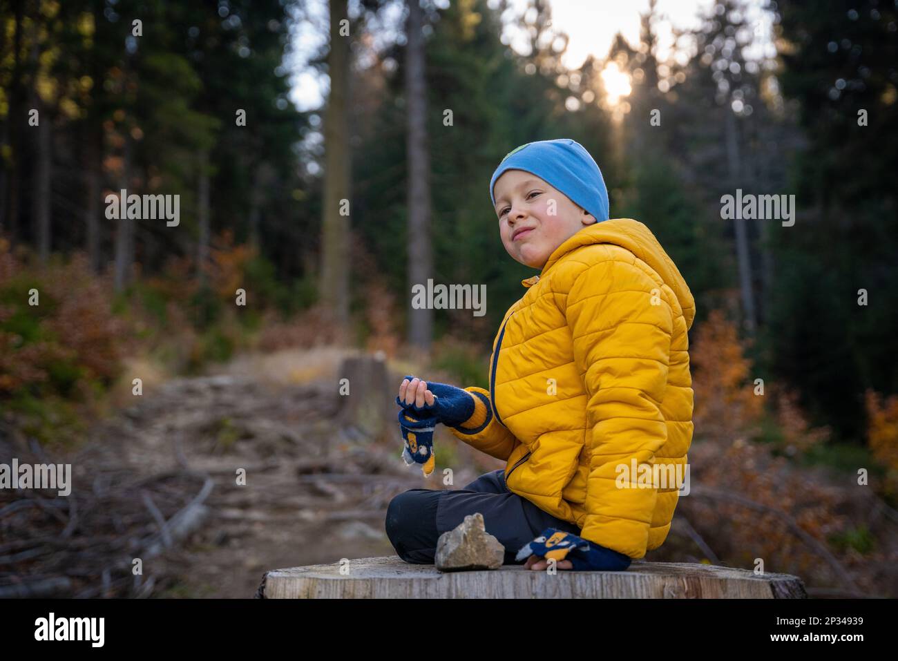 Little kid is sitting on a big stump on the mountain trail, eating ...