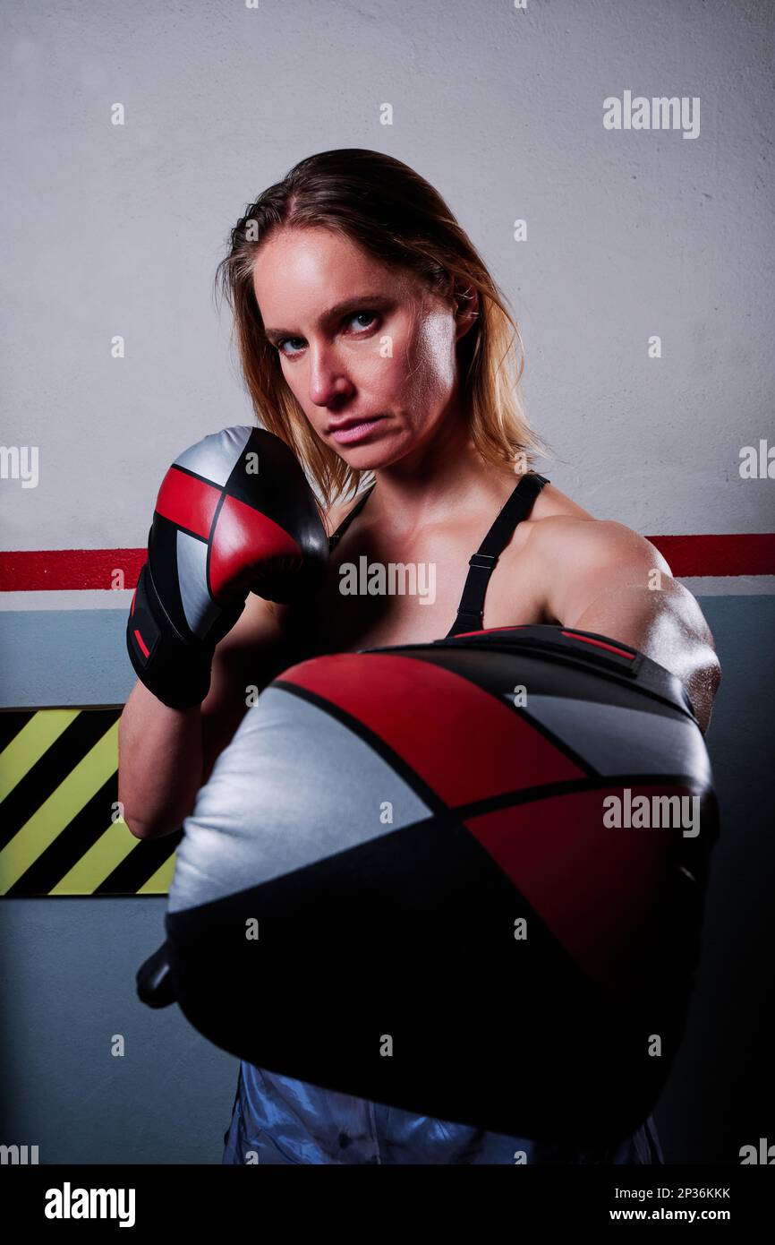 Female boxer looking at camera while posing with boxing gloves indoors ...