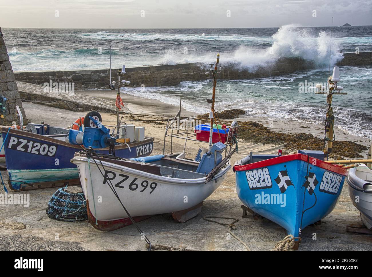 Fishing boats in coastal village, with waves crashing over breakwater ...
