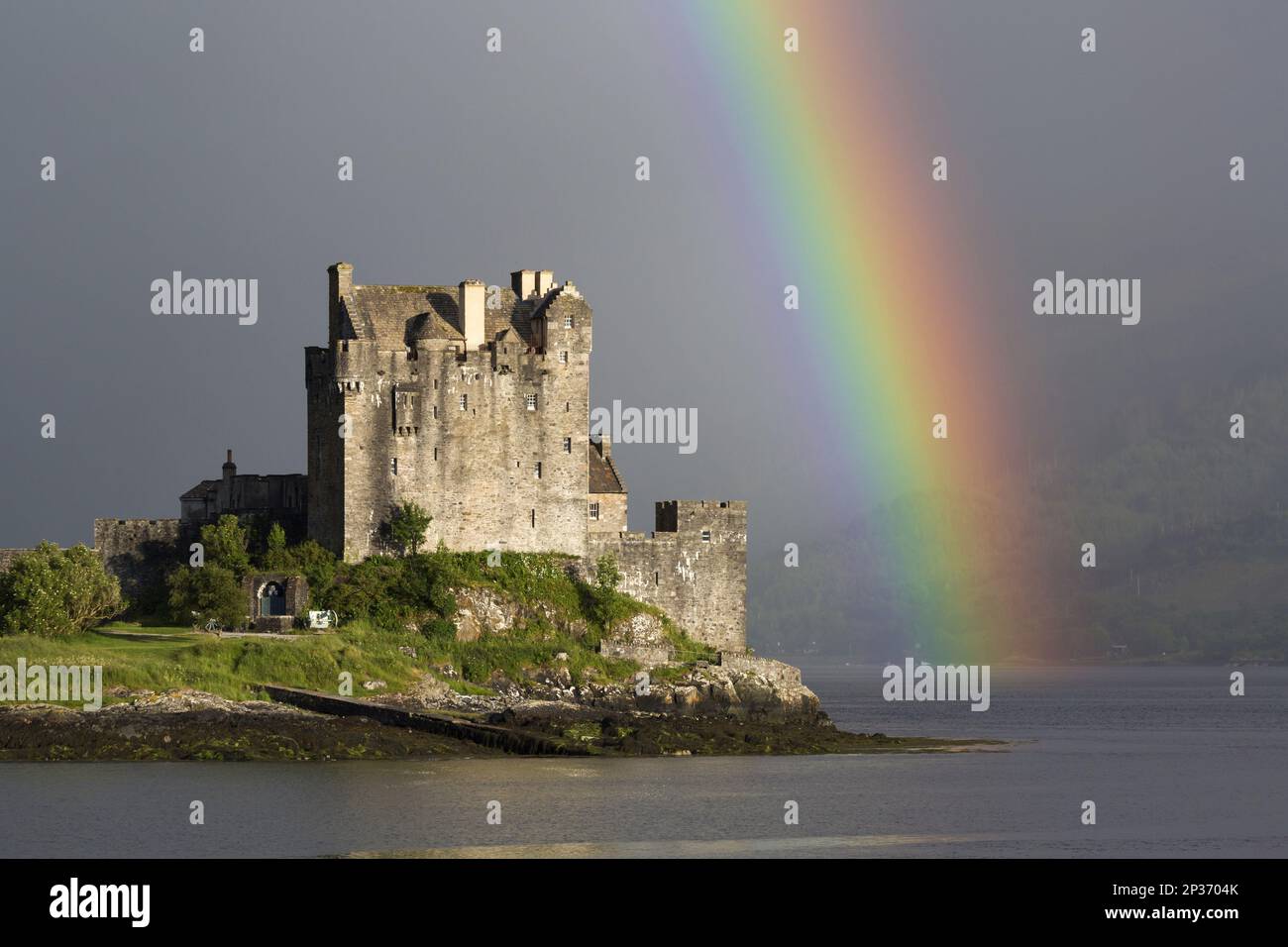 View of restored castle on tidal island in sea loch with rainbow, in ...