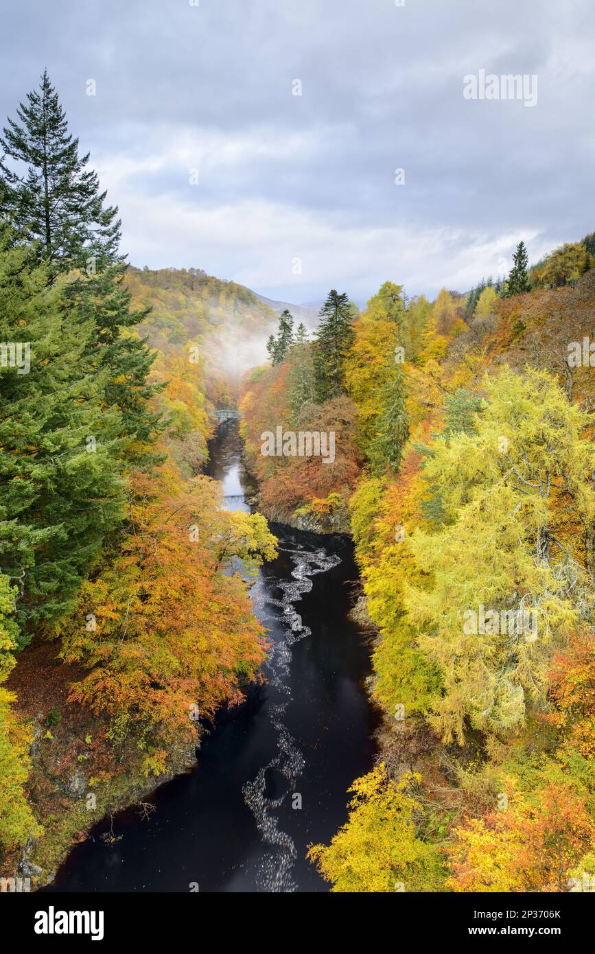 View of river flowing through mixed woodland in autumn colours ...