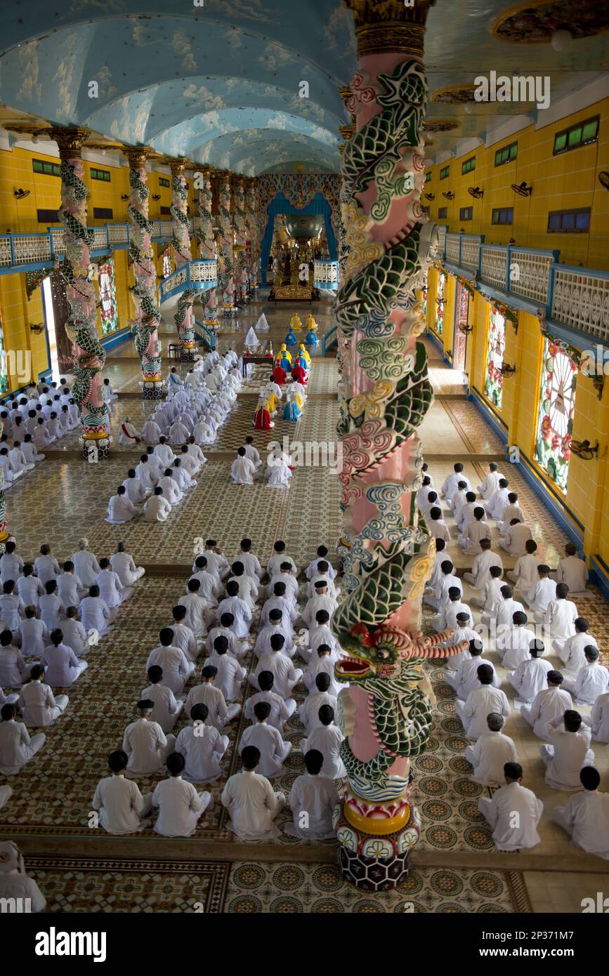 Caodaist disciples sitting beside colourful columns with dragons during ...