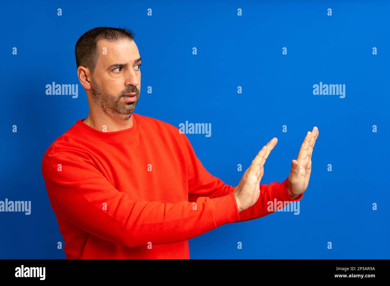Side view of scared bearded man in beige turtleneck raising hands in ...