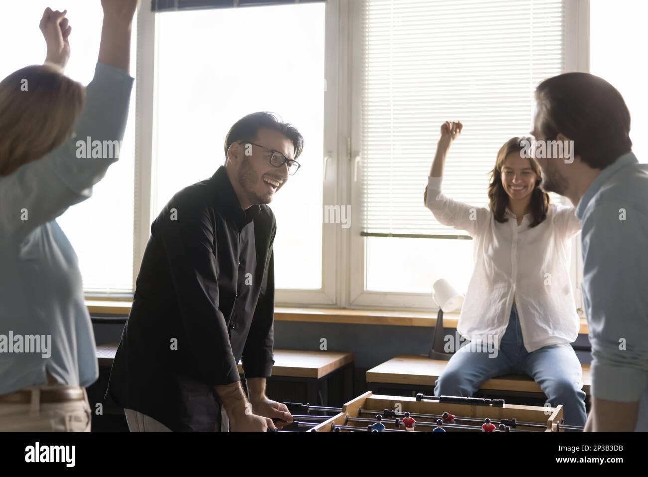 Cheerful millennial businessman beating colleague man in table soccer ...