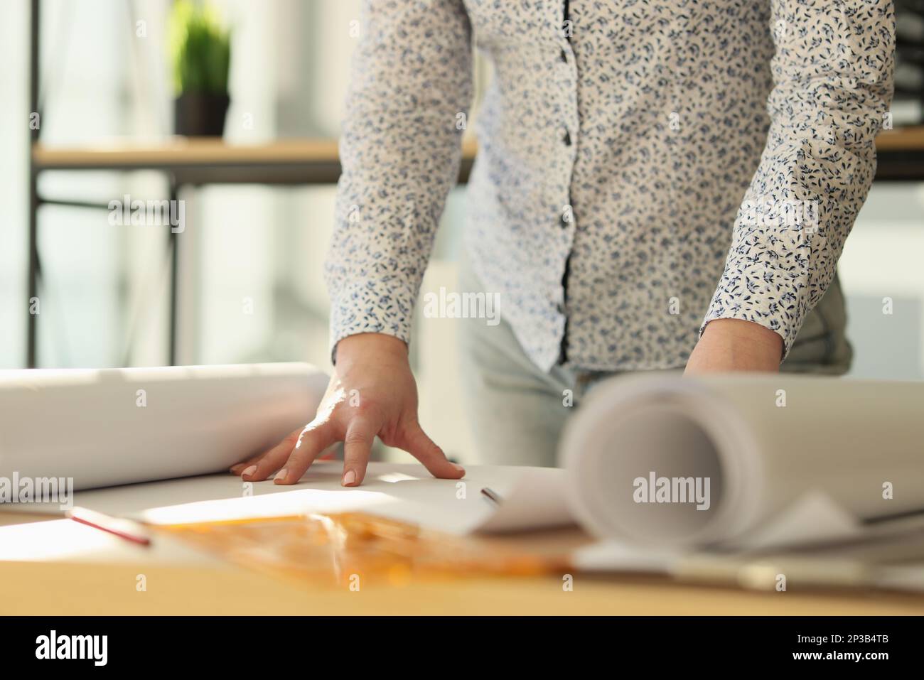 Female designer is standing near her work desk with rolls of paper ...