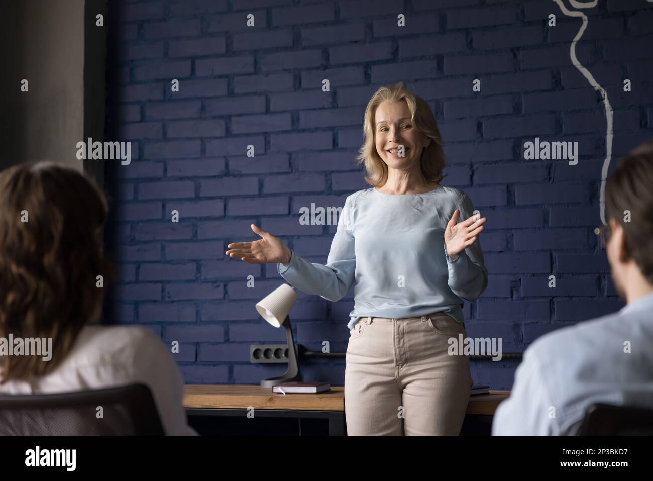 Friendly positive senior corporate teacher woman speaking before group ...