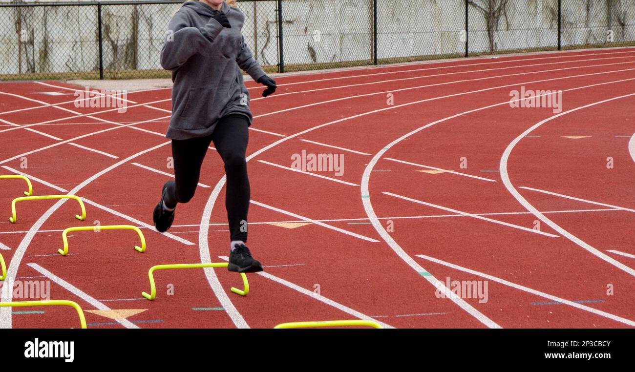 A high school female track runner running over yellow mini hurdles in winter outdoor during ...