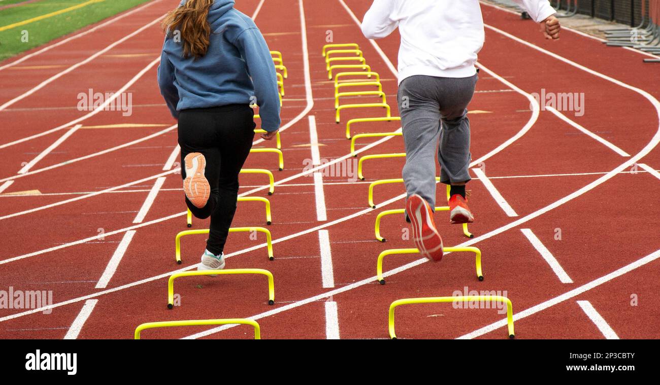Rear view of two track athletes running over small yellow hurdles in ...