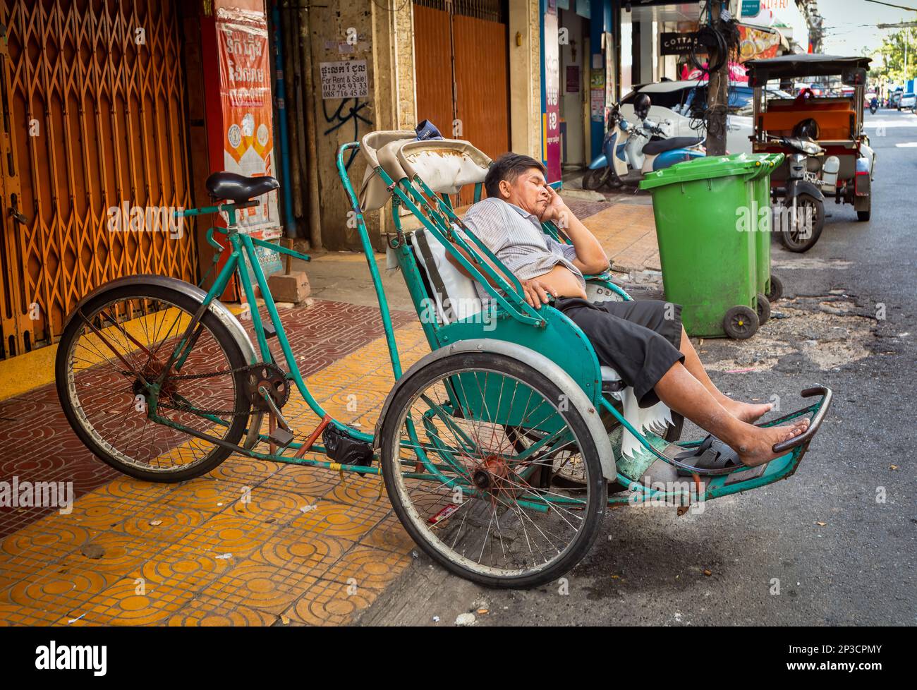 A traditional cyclo driver has a sleep in his pedicab down a side road ...