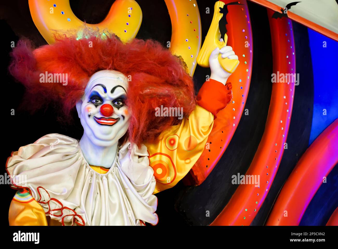 A smiling clown doll looks into the camera with a gun raised up in her ...