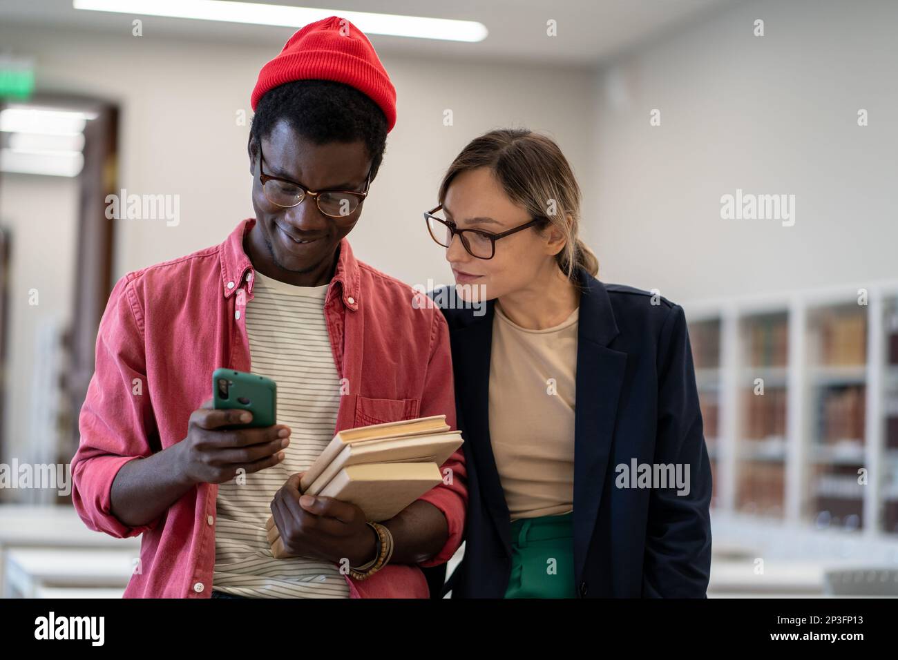 Two diverse students standing in classroom using smartphone during ...