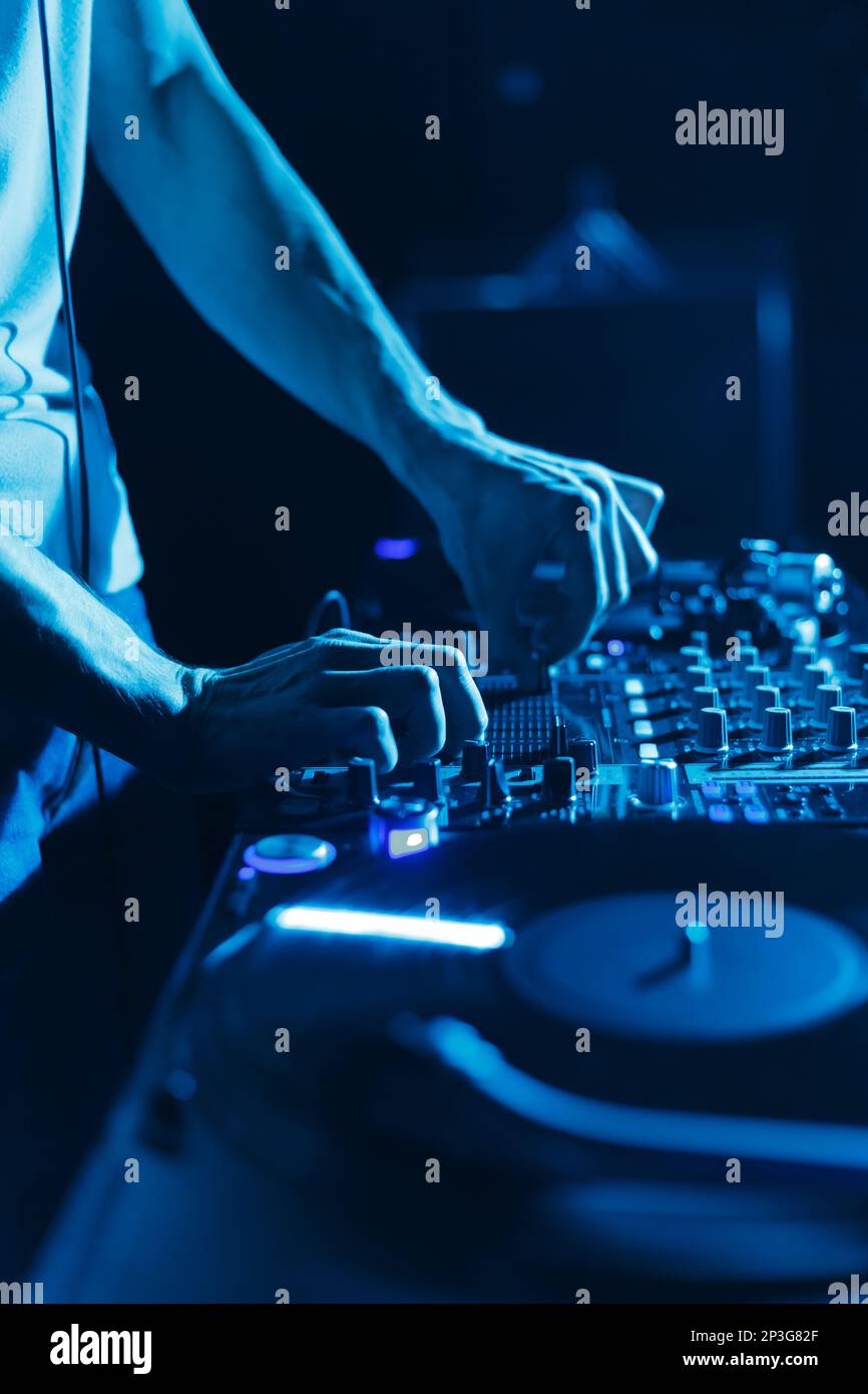 Club DJ mixing vinyl records in blue stage lights. Close up photo of ...