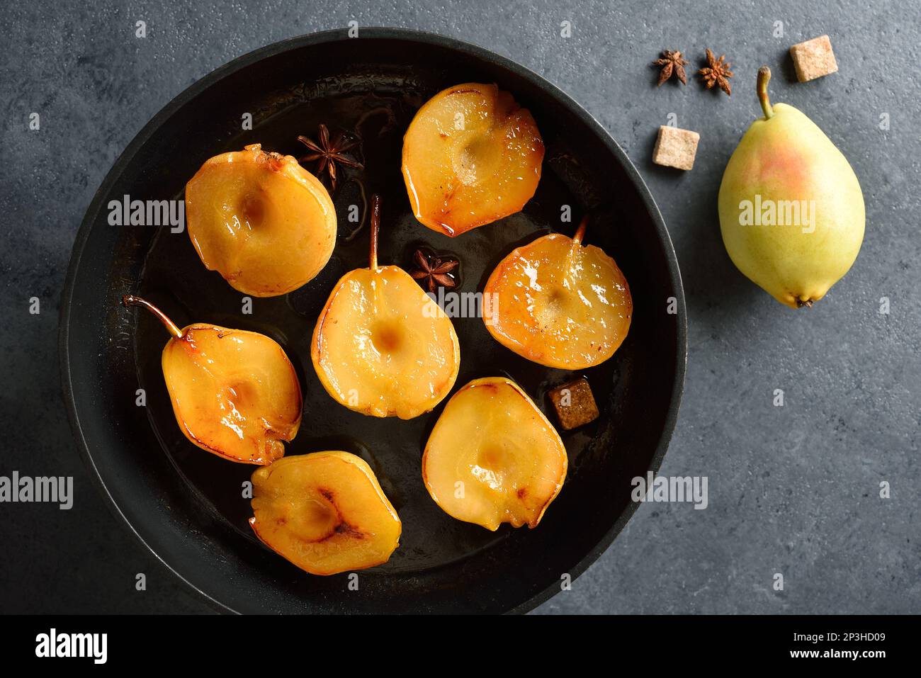 Vanilla poached pears in pan over dark stone background. Top view, flat ...