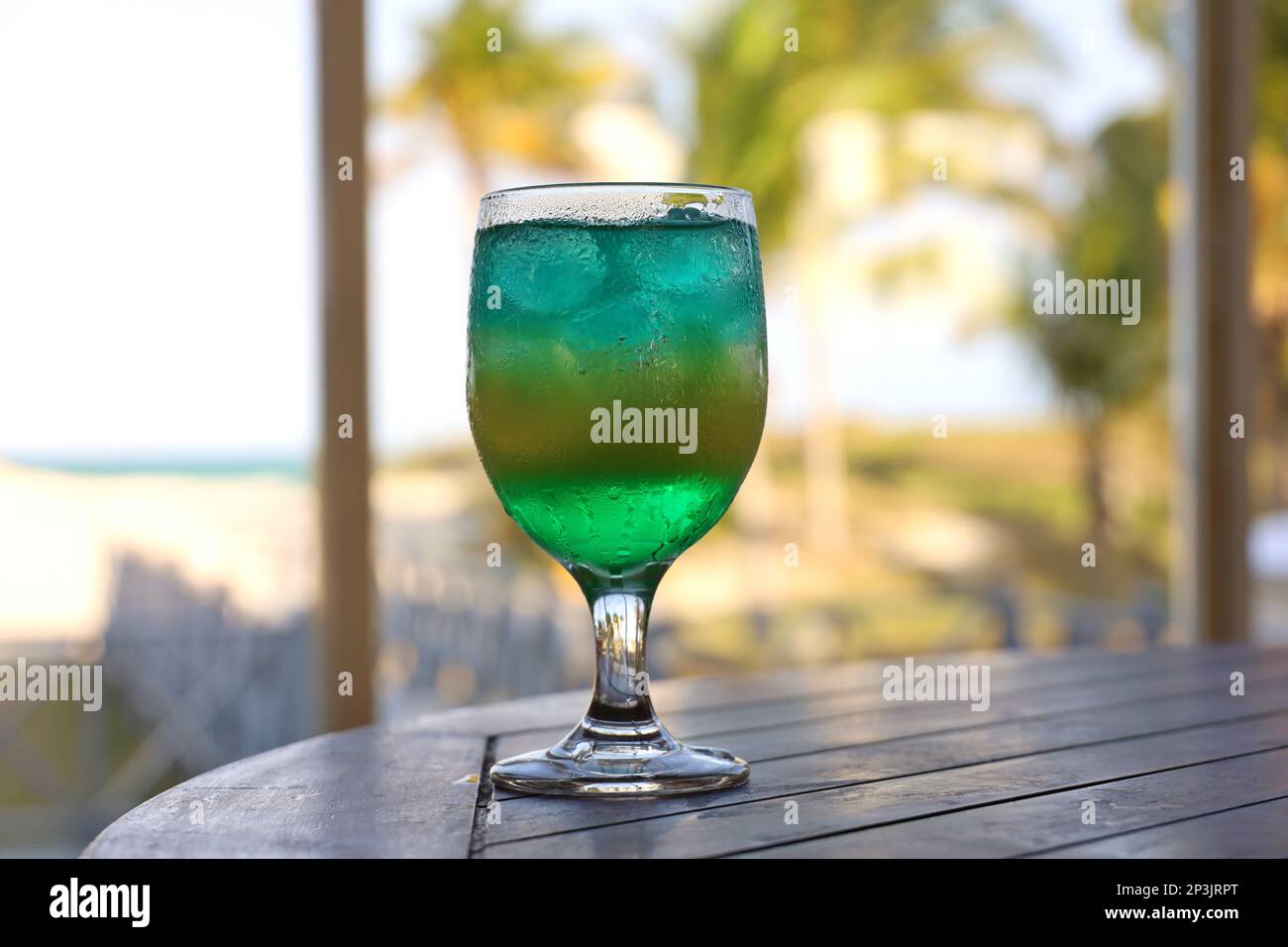 Glass with cool cocktail on wooden table on palm trees background. Sea ...