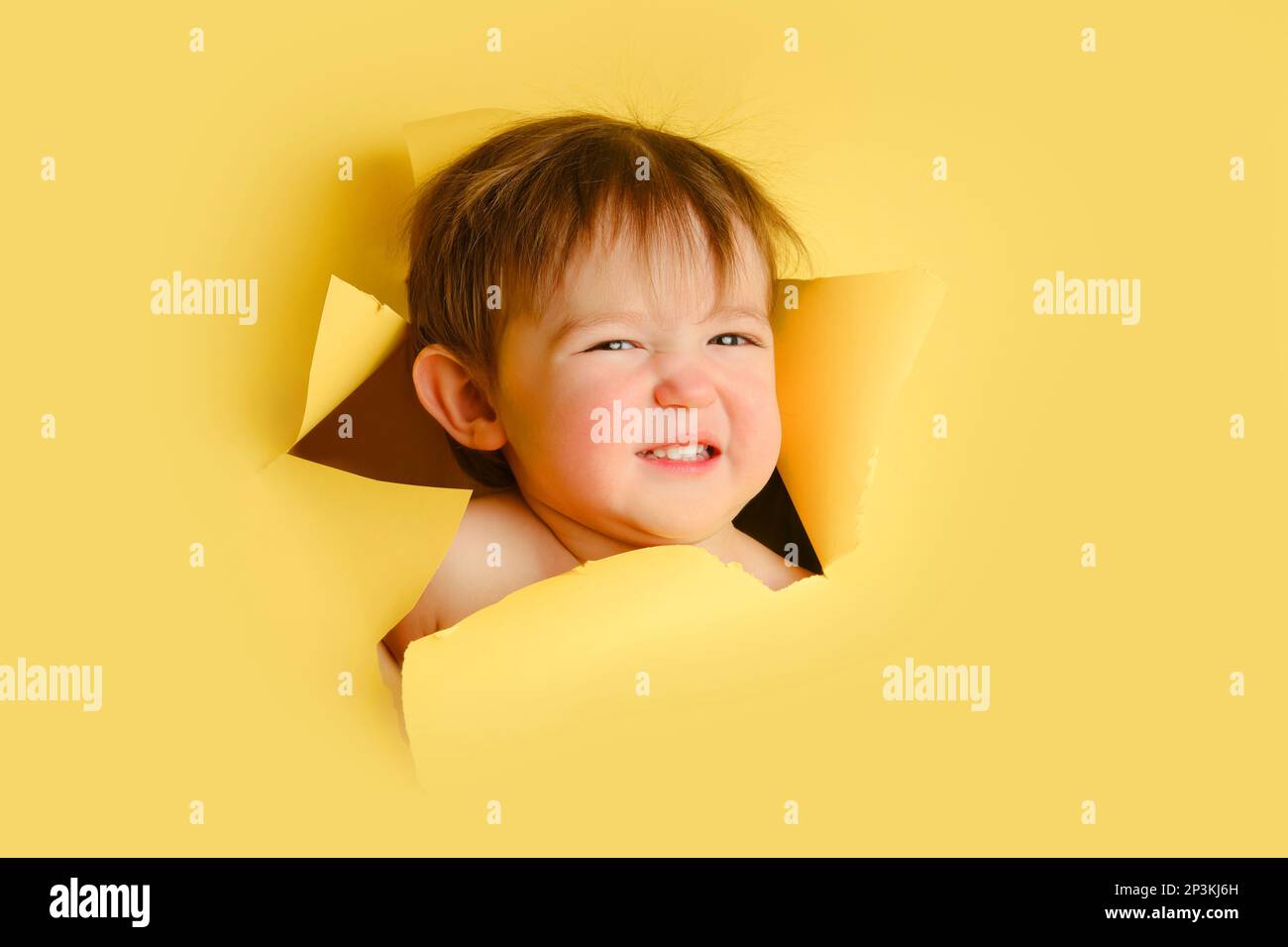 Shame baby in a hole on a paper yellow background. Torn child's head ...