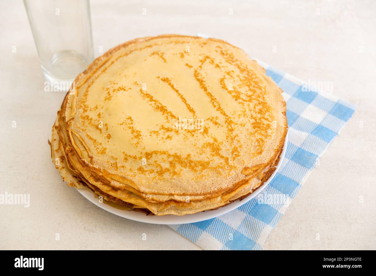 A stack of freshly baked pancakes and empty glass on a blue and white ...