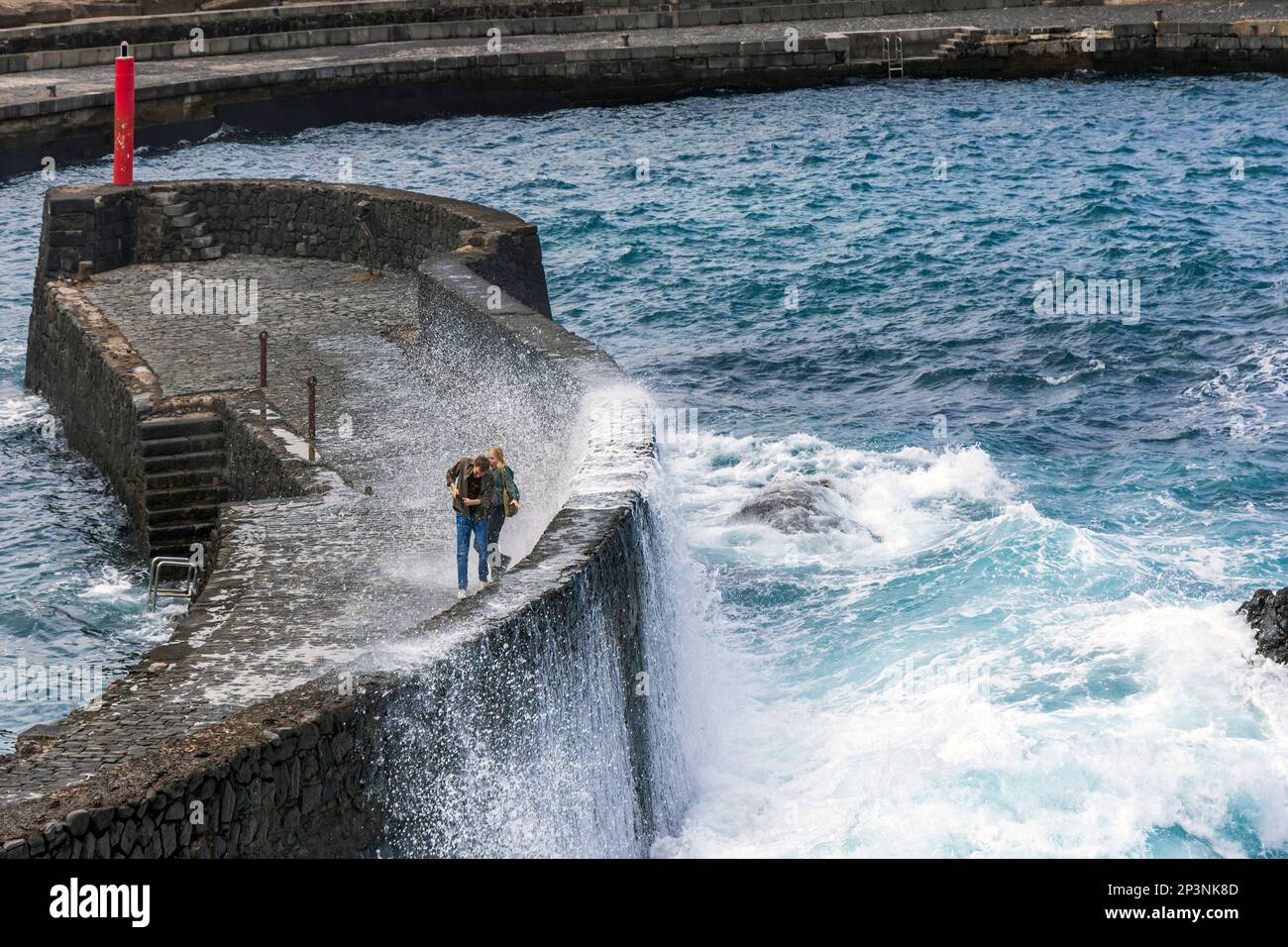 Two people getting wet by crashing wave at the harbour entrance and ...