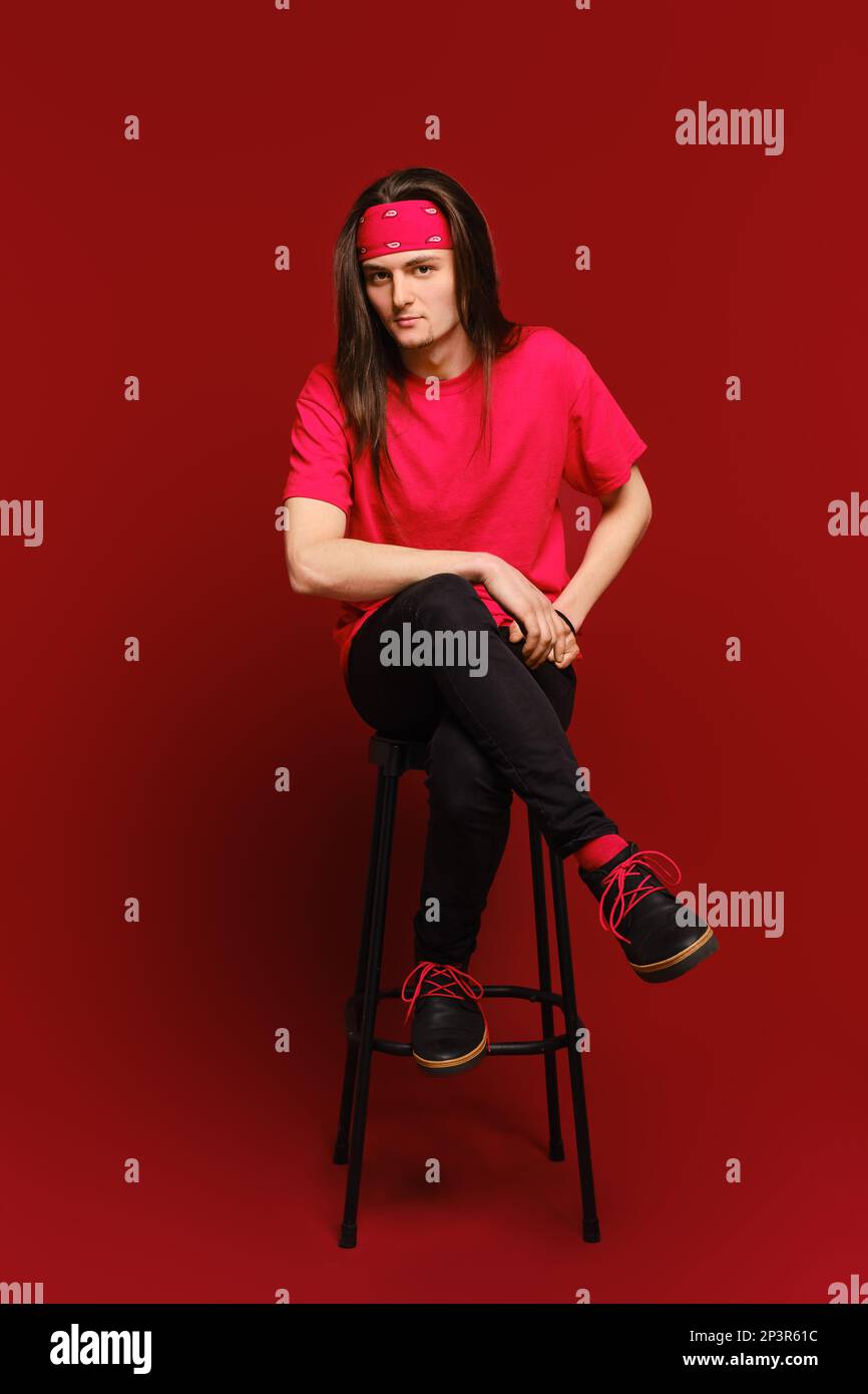 Young adult man sits on high stool with his leg on another leg and ...