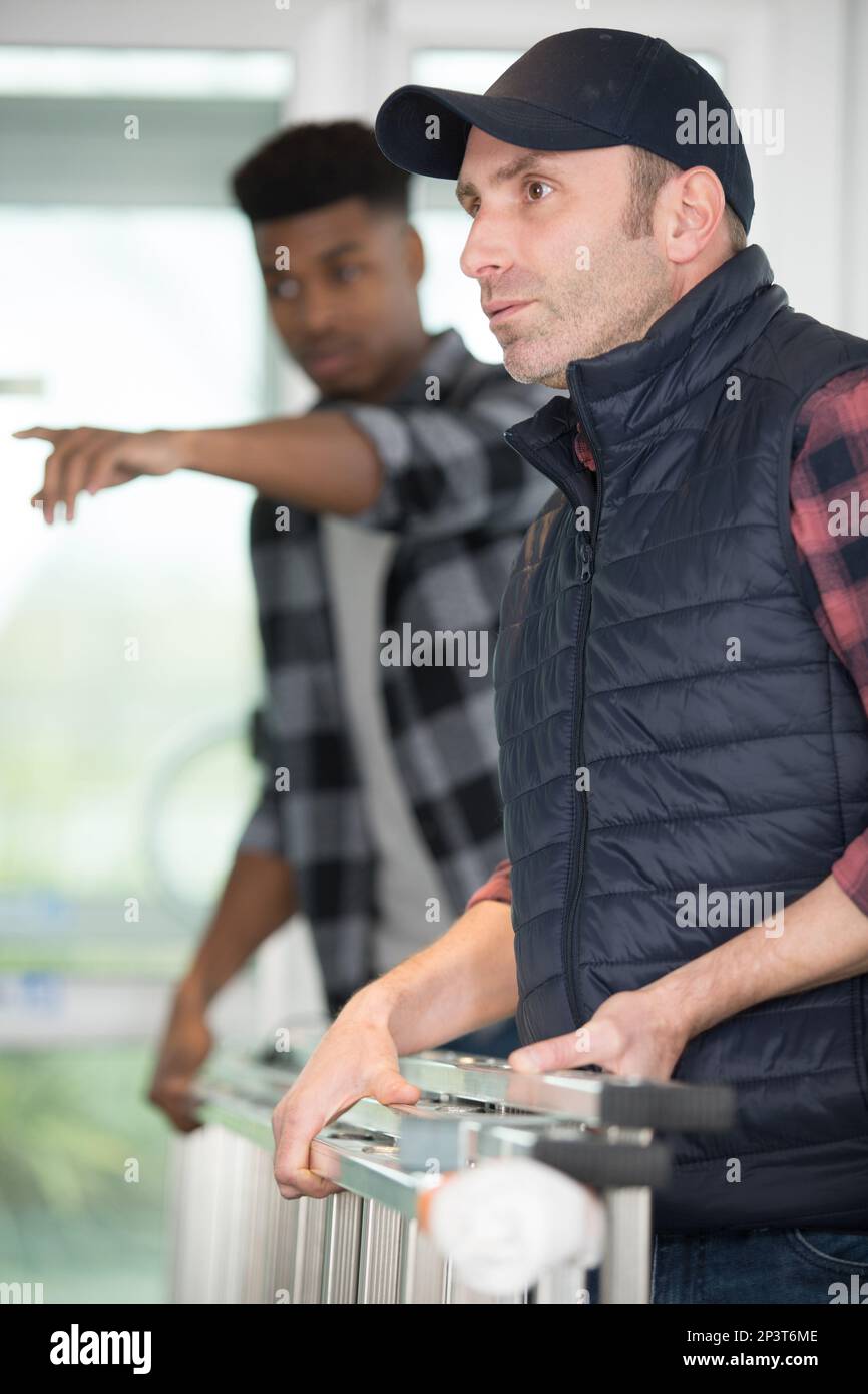 view of construction workers carrying ladder together Stock Photo - Alamy