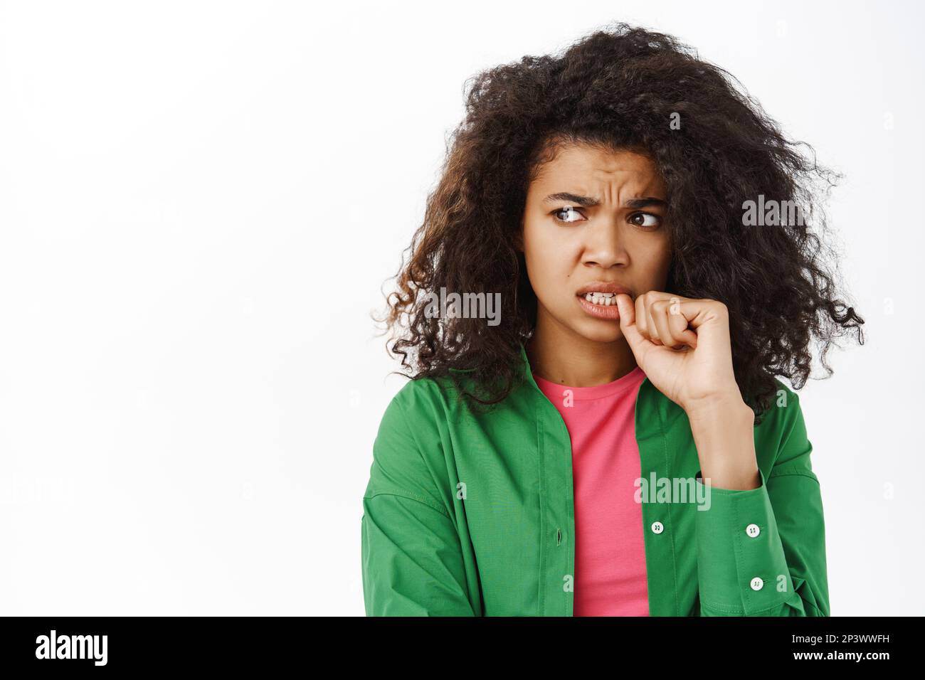 Portrait of complicated young woman, biting finger nail and looks ...