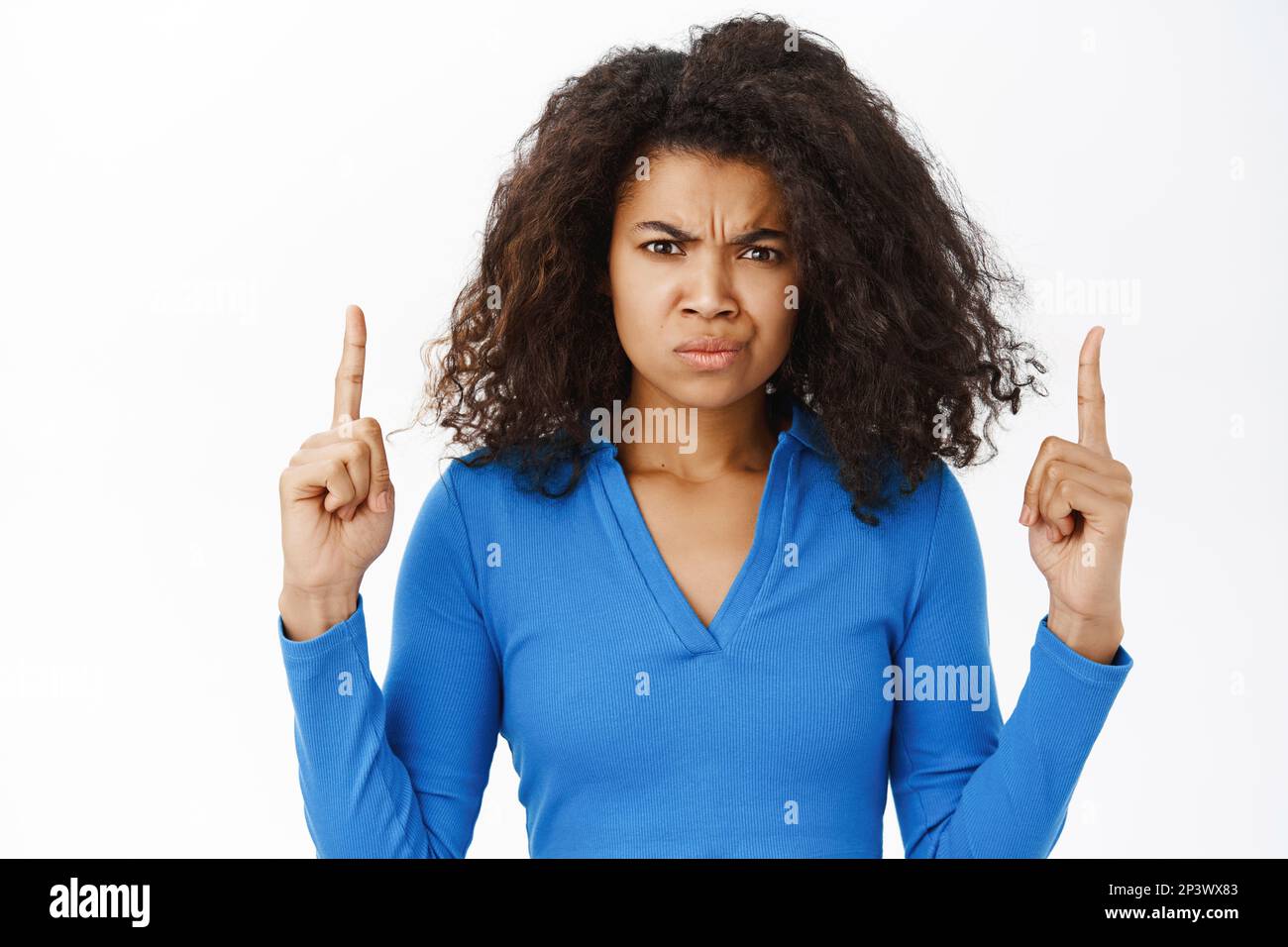 Portrait of angry and confused girl points up, frowns and looks puzzled ...