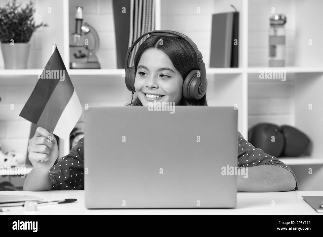 A young school girl student sitting at the table, using laptop when ...
