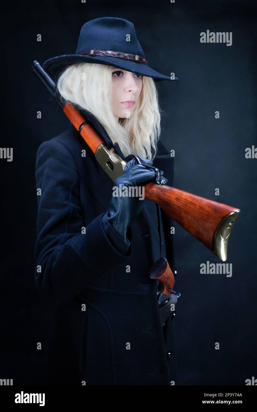 old west blonde girl wearing black hat with gun on black background Stock Photo - Alamy