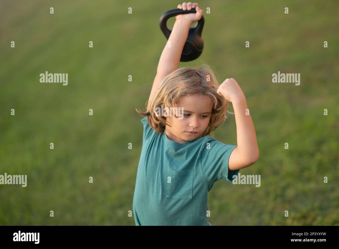 Child lifting the kettlebell in park outside. Cute child boy pumping up ...