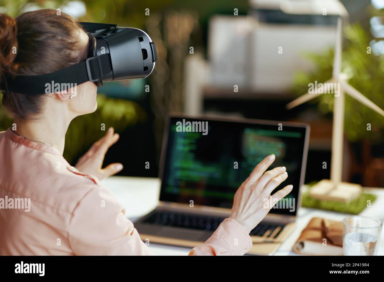 Seen from behind modern woman with laptop and virtual reality headset ...