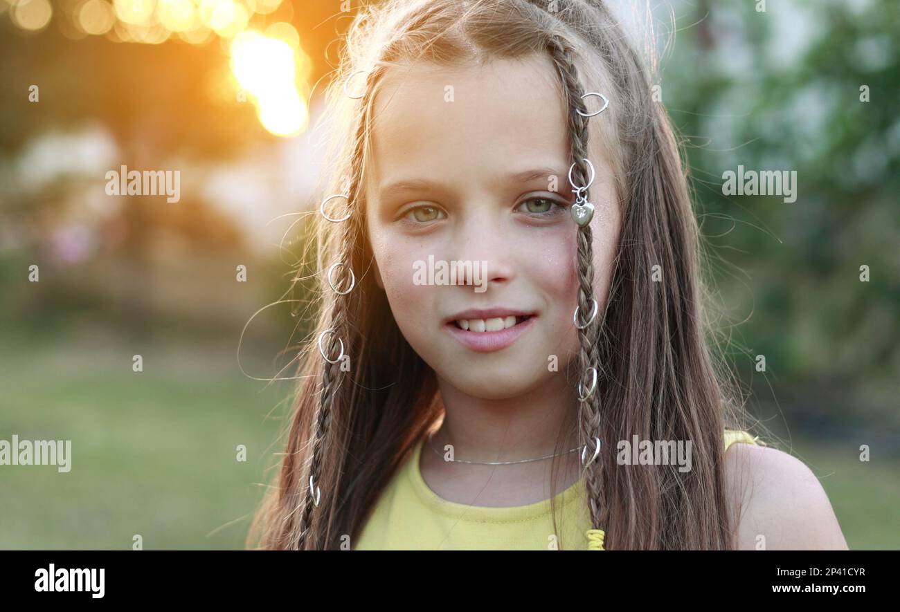 front view of adorable little girl with hairstyle is smiling with her outdoors on summer day ...