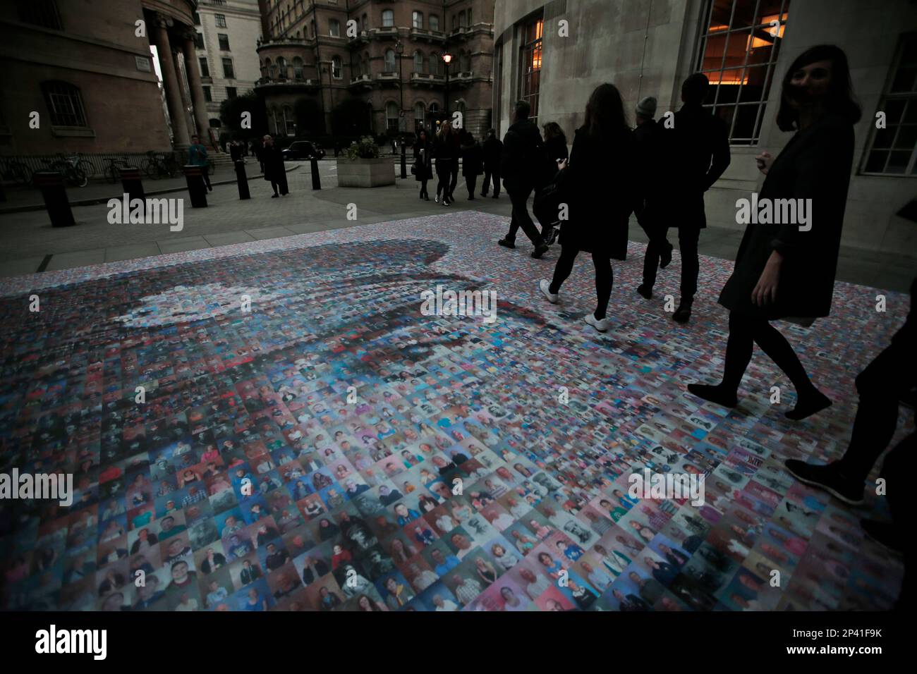 People walk on a digital mosaic of photographs of people, depicting ...