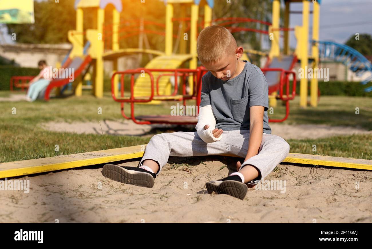 crying child with broken limb arm sits outdoors and looking how kid ...