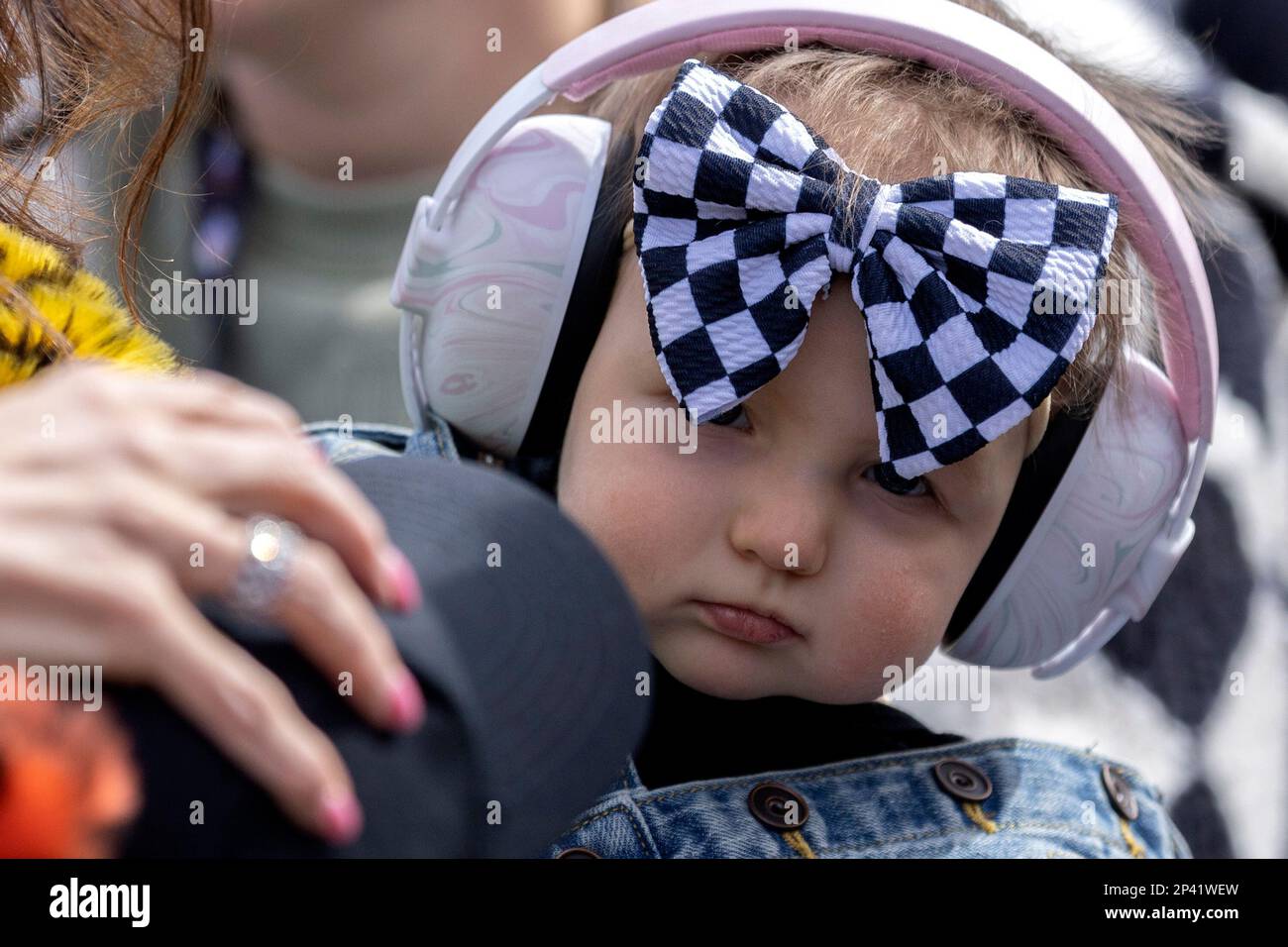 A young fan wears a checkered bow and ear muffs to protect from noise ...