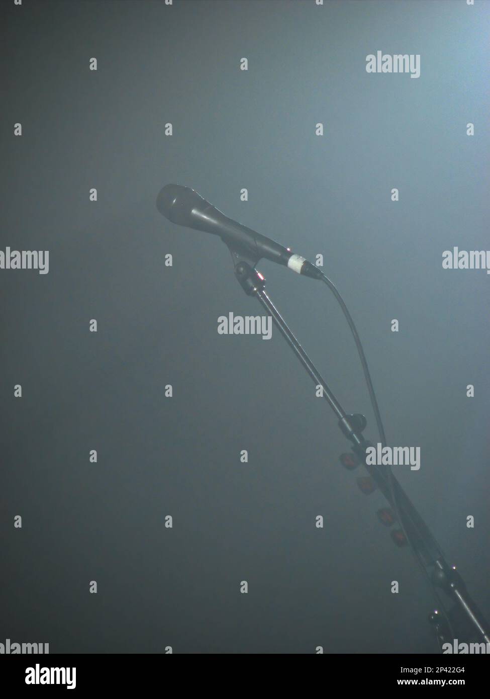 A wired singer's microphone on a stand with white light streaming ...