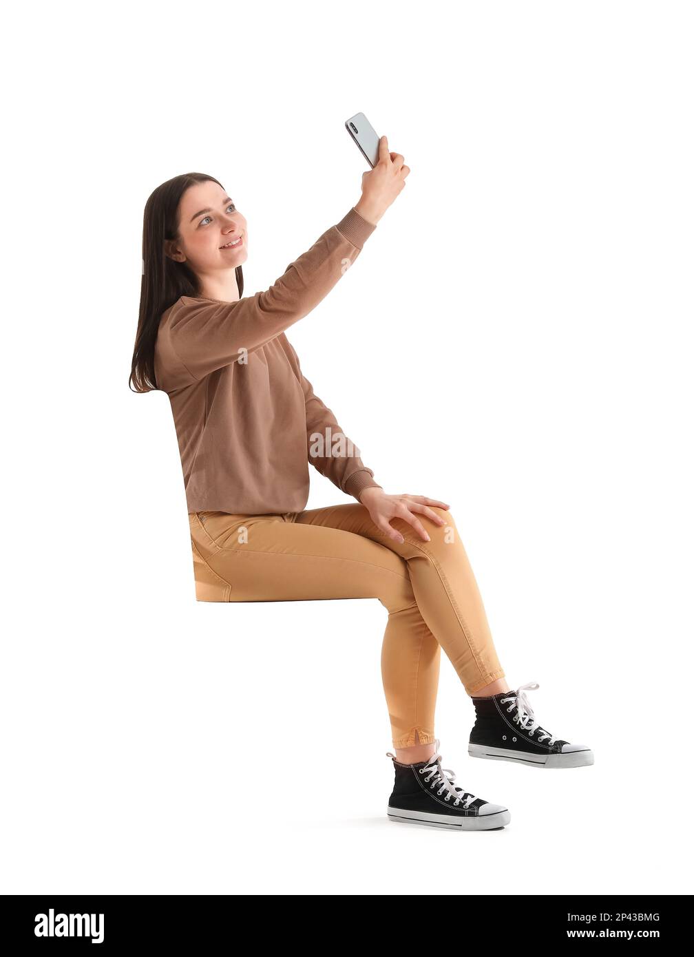 Pretty young woman with smartphone taking selfie while sitting on chair ...