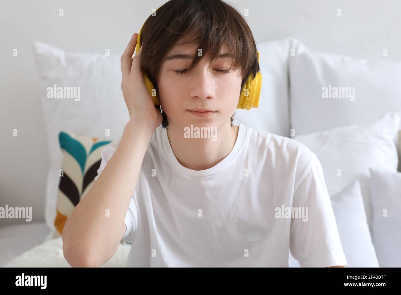 Teenage boy with headphones listening to music in bedroom, closeup ...