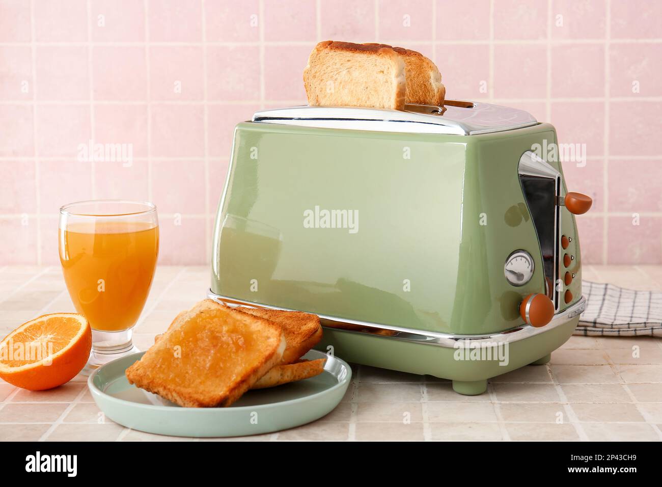 Bread slices in modern toaster, cup of juice, orange and toasts with jam on tile table Stock ...
