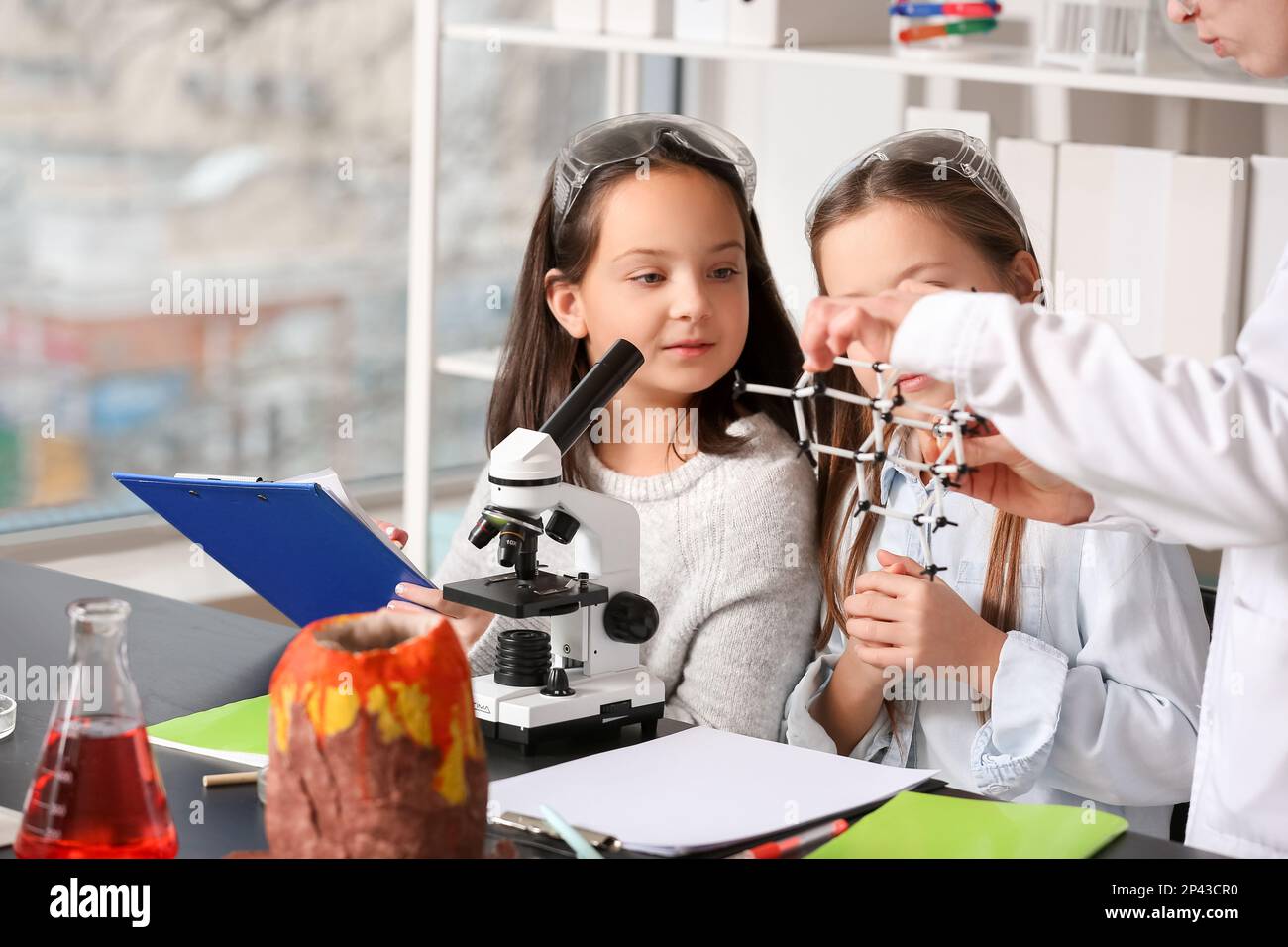 Chemistry teacher with molecular model conducting lesson to little girls in science classroom ...