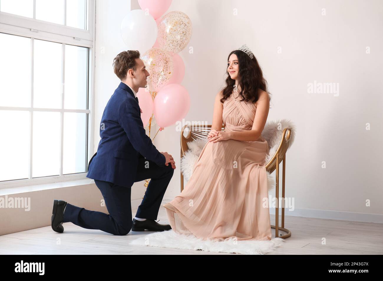 Teenage boy standing on one knee in front of his prom date at home ...