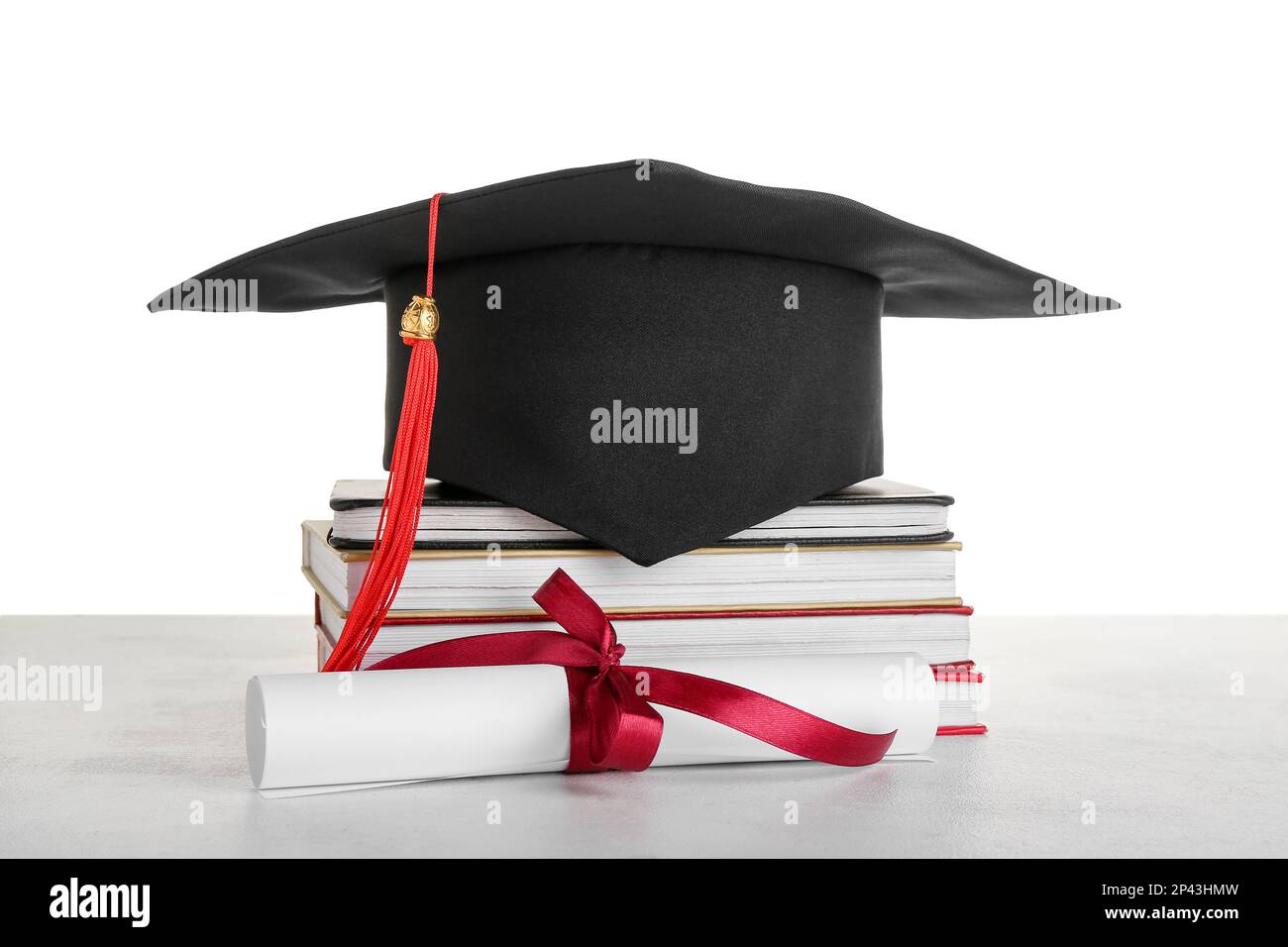 Graduation hat with diploma and books on table against white background ...