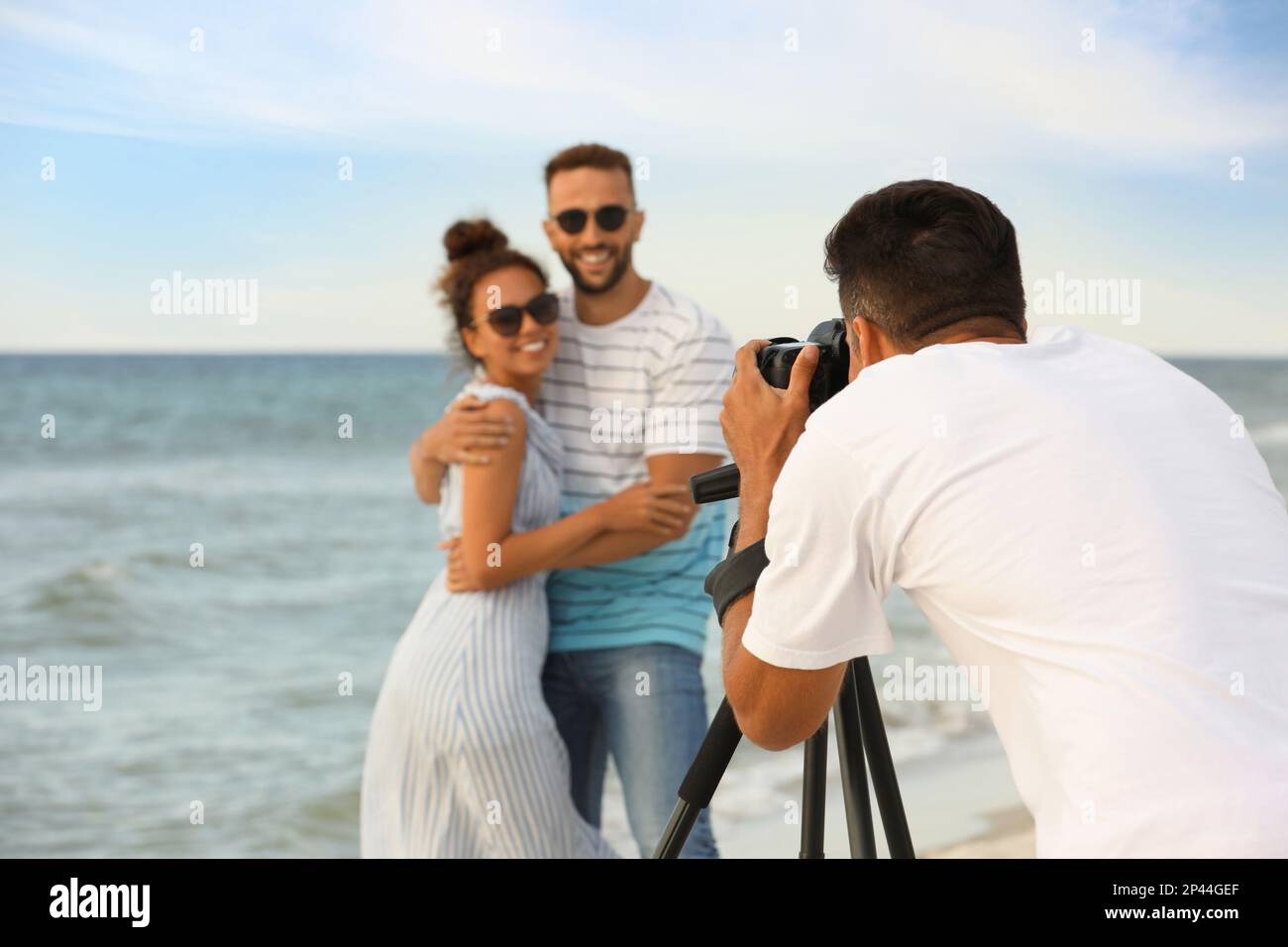 Photographer taking picture of couple with professional camera near sea ...