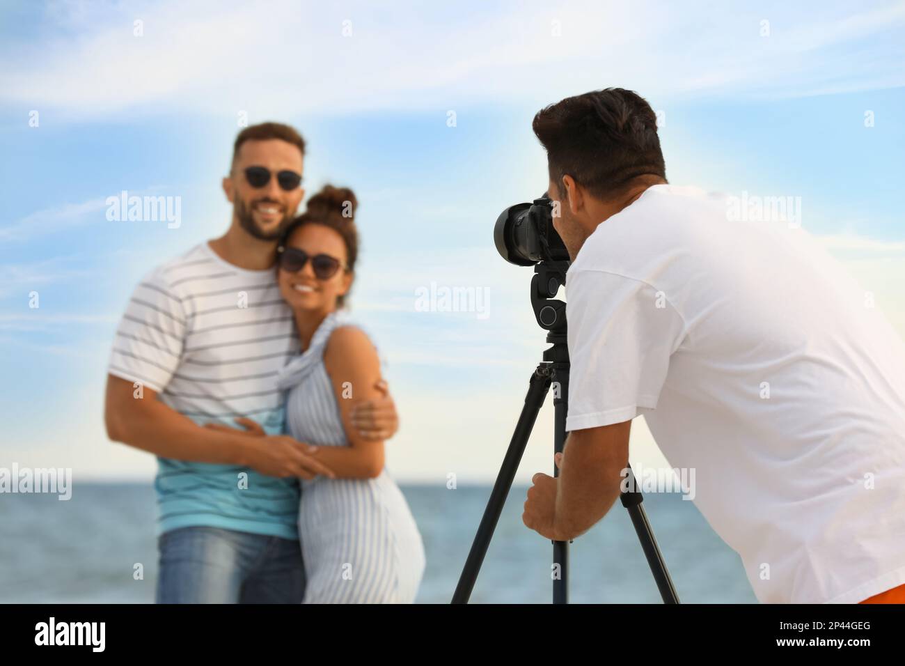 Photographer taking picture of couple with professional camera near sea ...