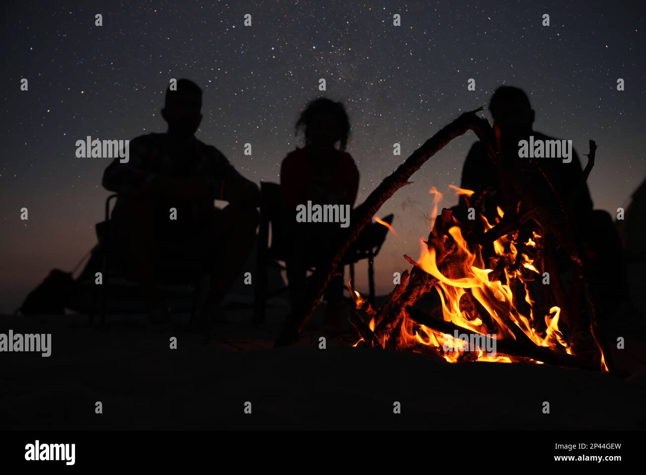 Group of friends gathering around bonfire in evening, focus on flame ...