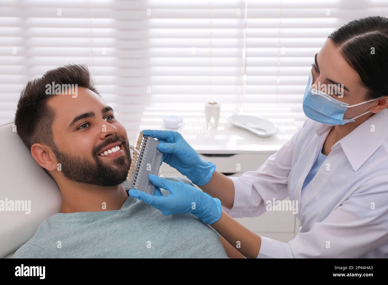 Dentist checking young man's teeth color in clinic Stock Photo - Alamy