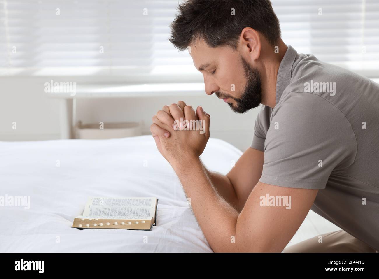 Religious man with Bible praying in bedroom Stock Photo - Alamy