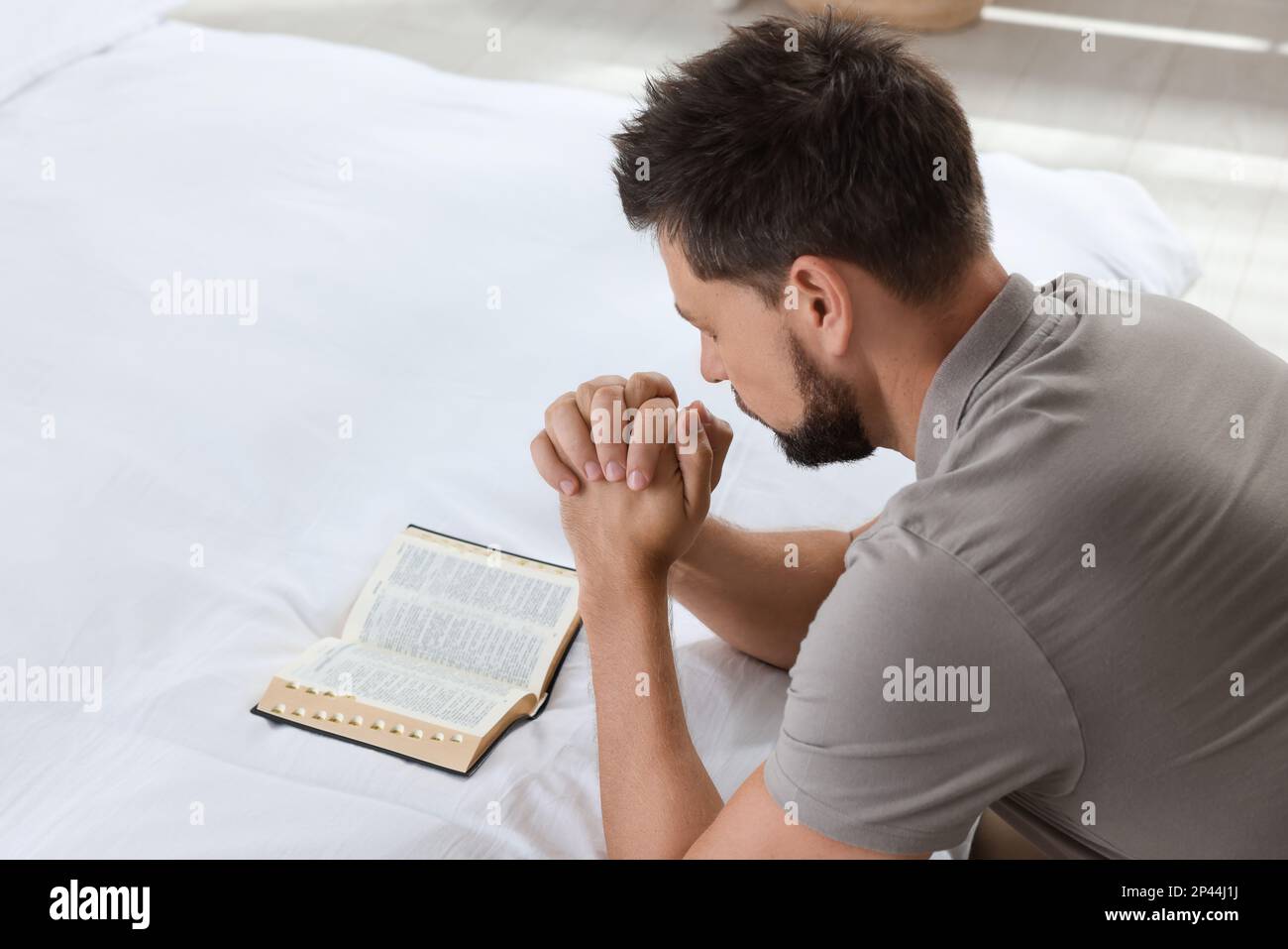 Religious man with Bible praying in bedroom Stock Photo - Alamy