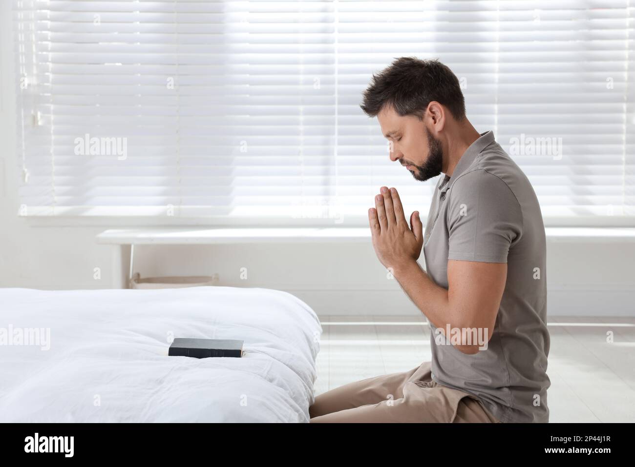 Religious man with Bible praying in bedroom Stock Photo - Alamy