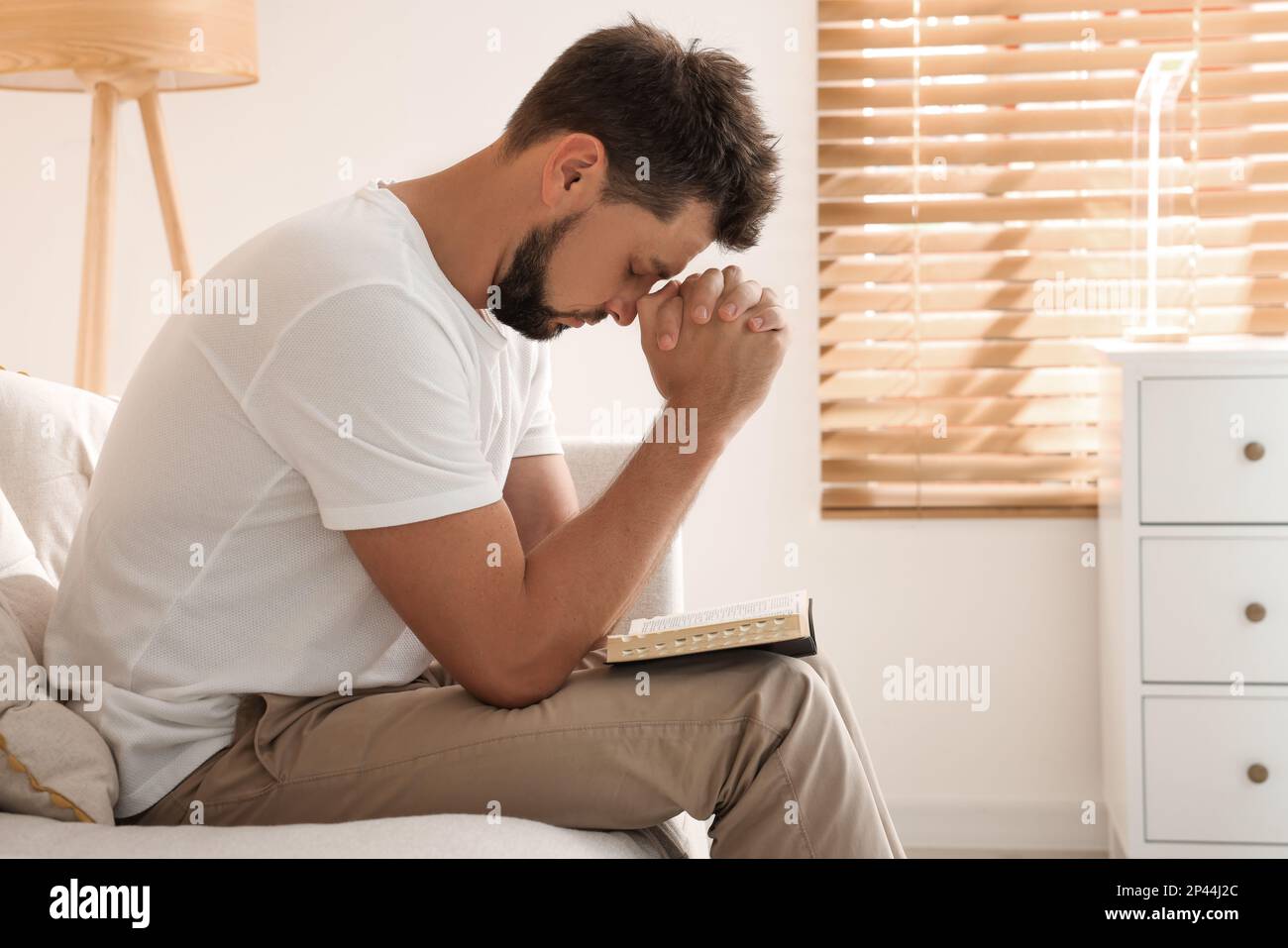 Religious man with Bible praying indoors. Space for text Stock Photo ...