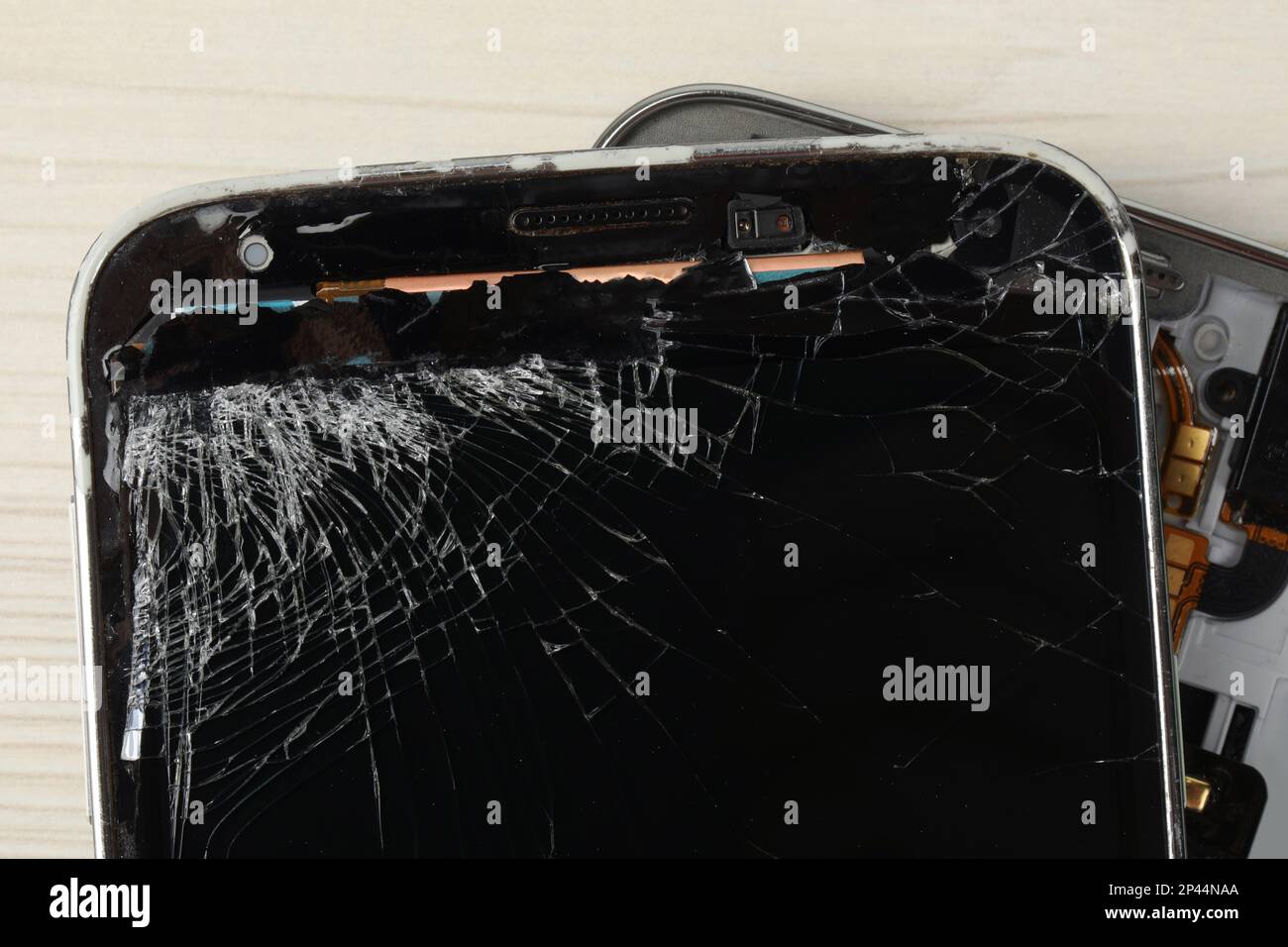Broken smartphone with cracked screen on light beige wooden background ...