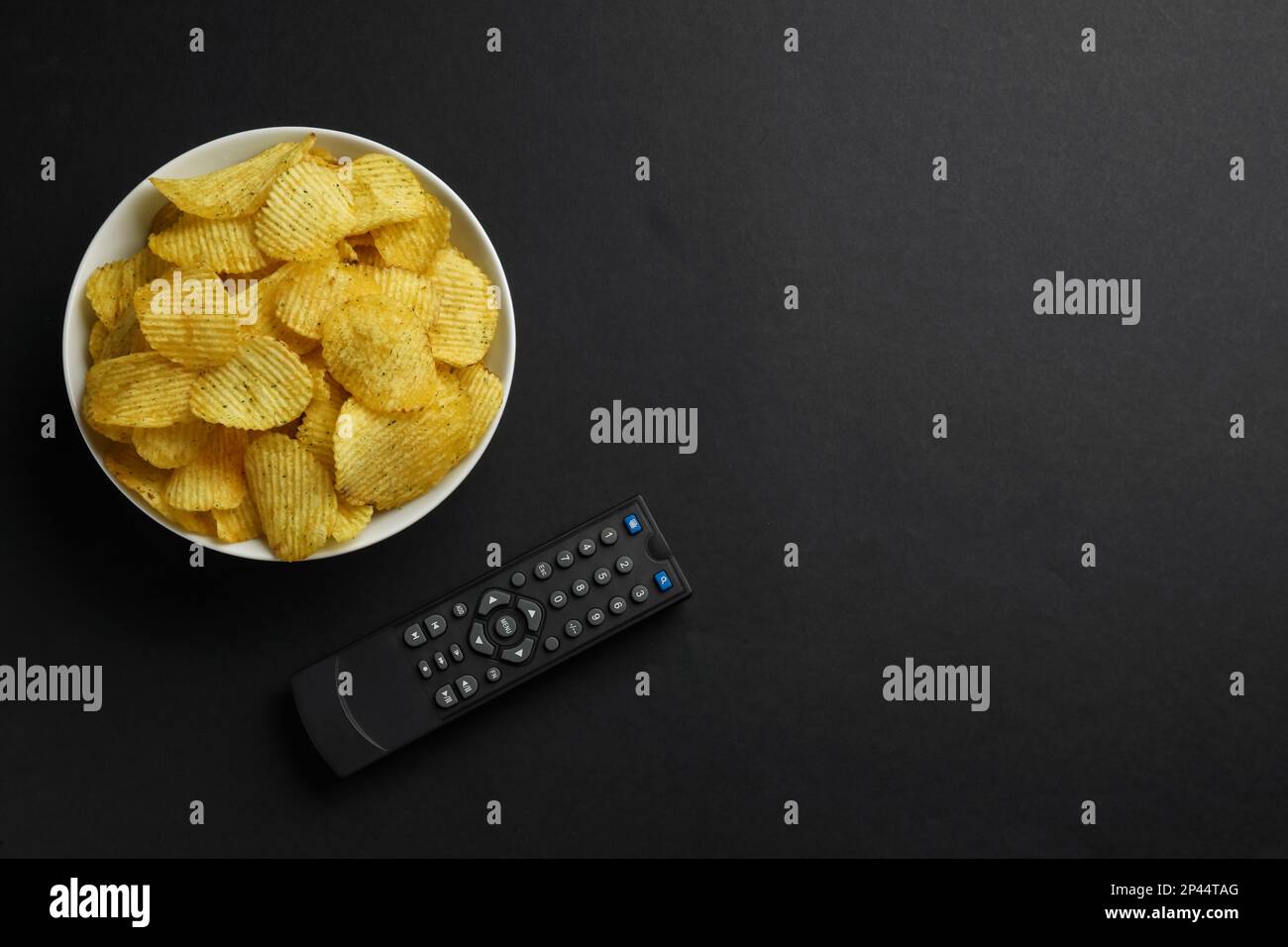 Modern tv remote control and chips on black background, flat lay. Space ...